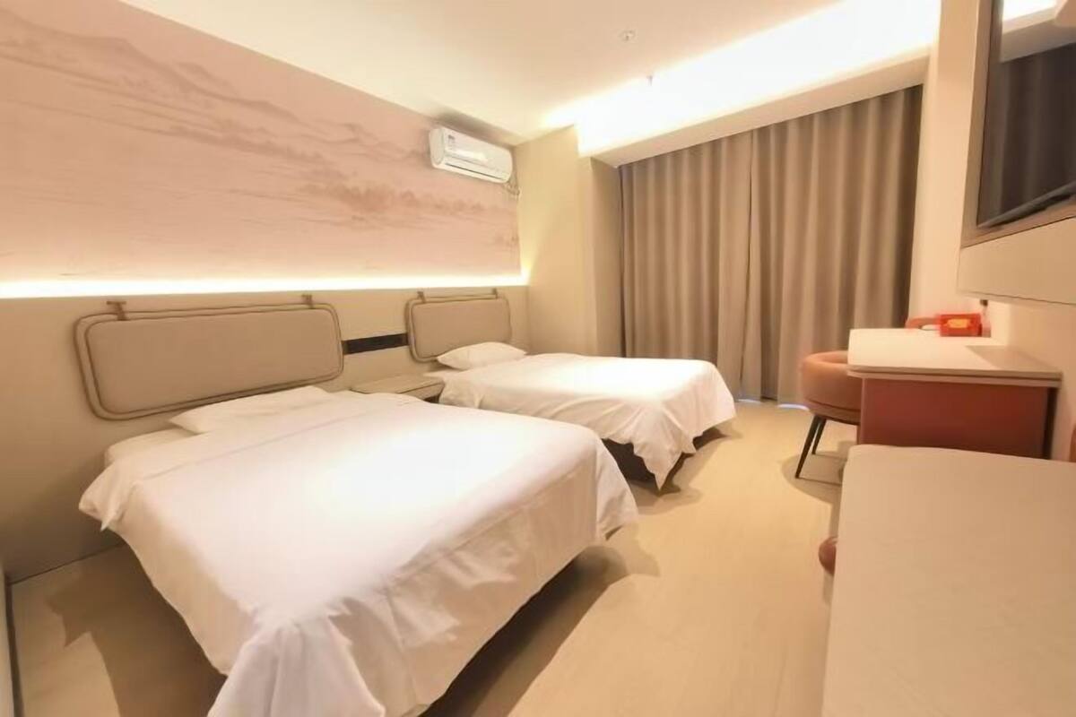 Quarto de hotel com duas camas, mesa de cabeceira, espelho e janela com cortinas.