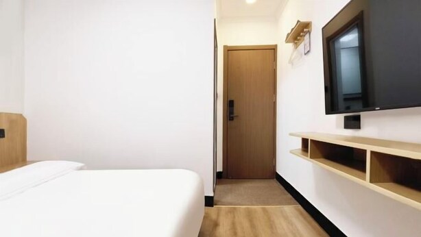 Quarto de hotel com uma cama, televisão na parede e porta que dá para outro aposento.