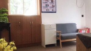 Quarto com um armário de madeira, uma escrivaninha branca, um sofá cinza e uma pequena mesa vermelha.