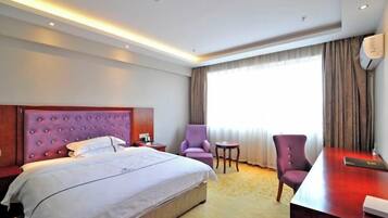 Quarto de hotel com uma cama grande, duas cadeiras, uma escrivaninha e uma janela com cortinas.