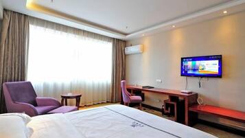Quarto de hotel com cama, escrivaninha, cadeira, televisão e janela com cortinas.
