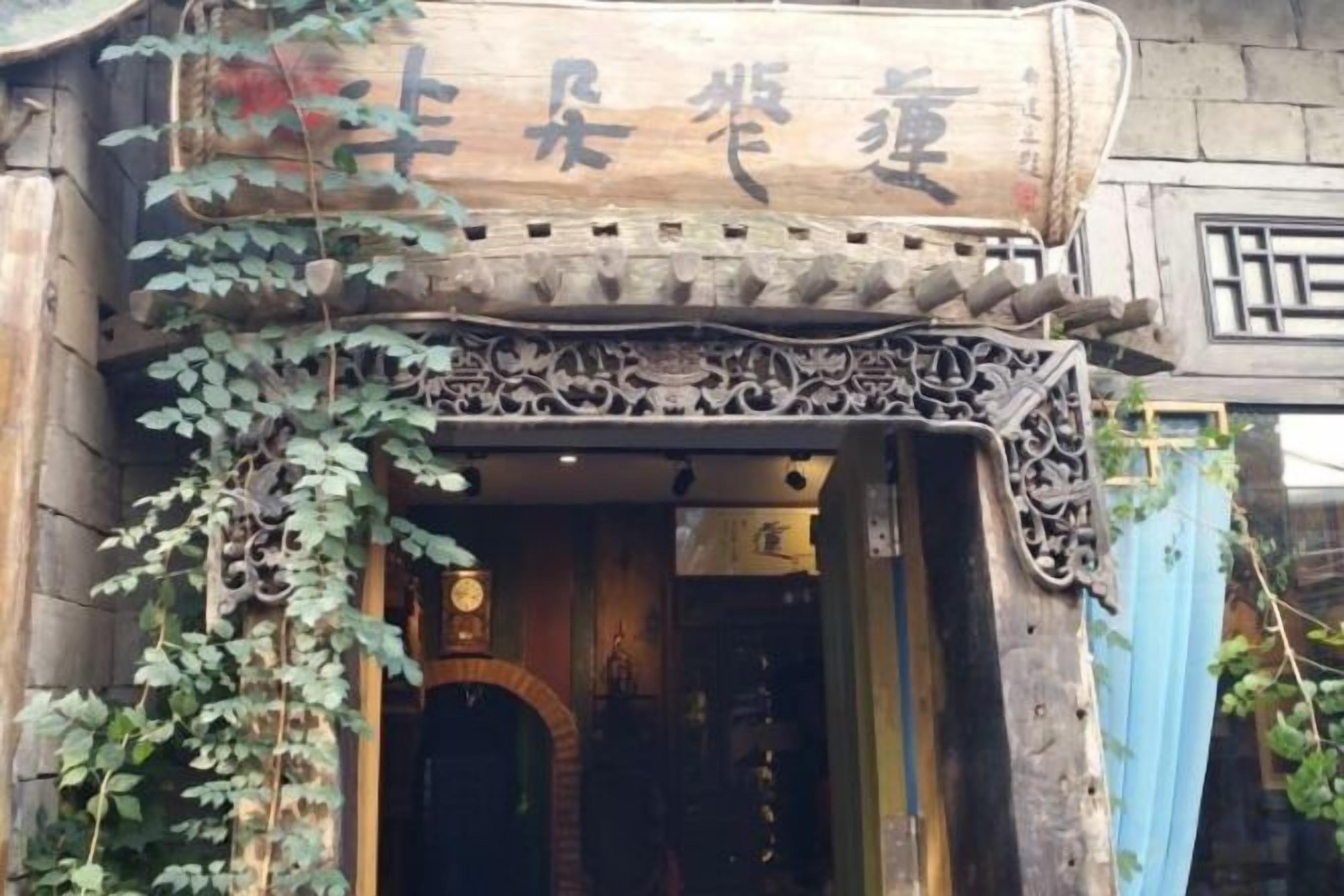 Entrada de um edifício tradicional com esculturas elaboradas e uma placa com caracteres chineses.