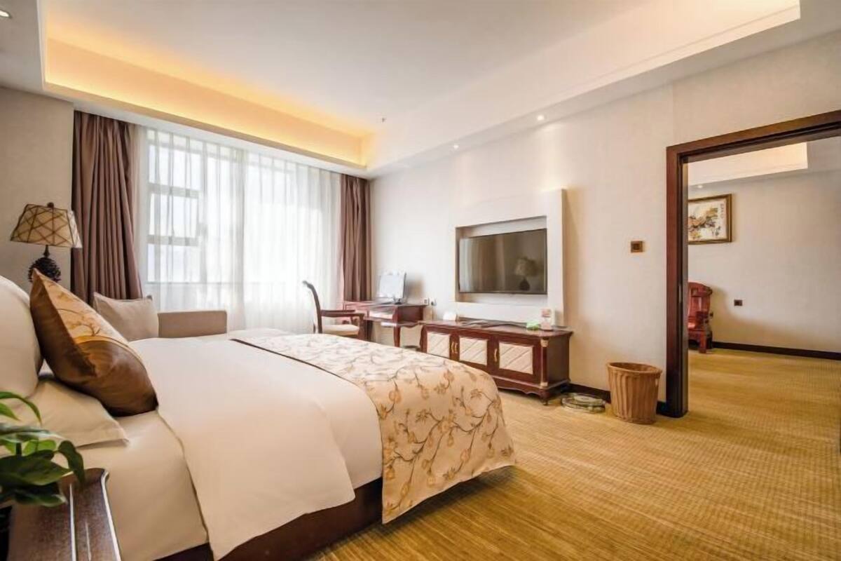 Quarto de hotel com cama, escrivaninha, televisão e vista para o exterior.