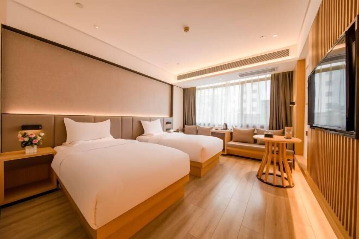 Quarto de hotel com duas camas, um sofá, uma televisão e uma mesinha.