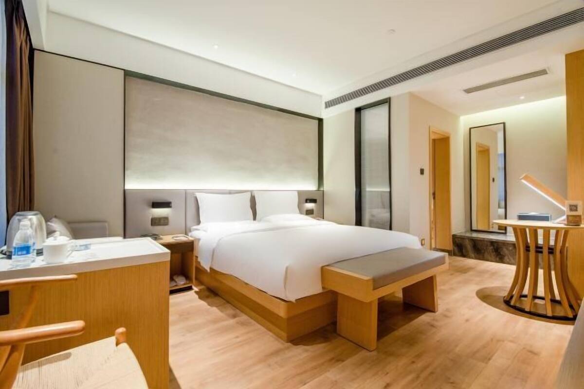 Quarto de hotel moderno com uma cama grande, mesa de cabeceira, escrivaninha e um pequeno espaço de estar.