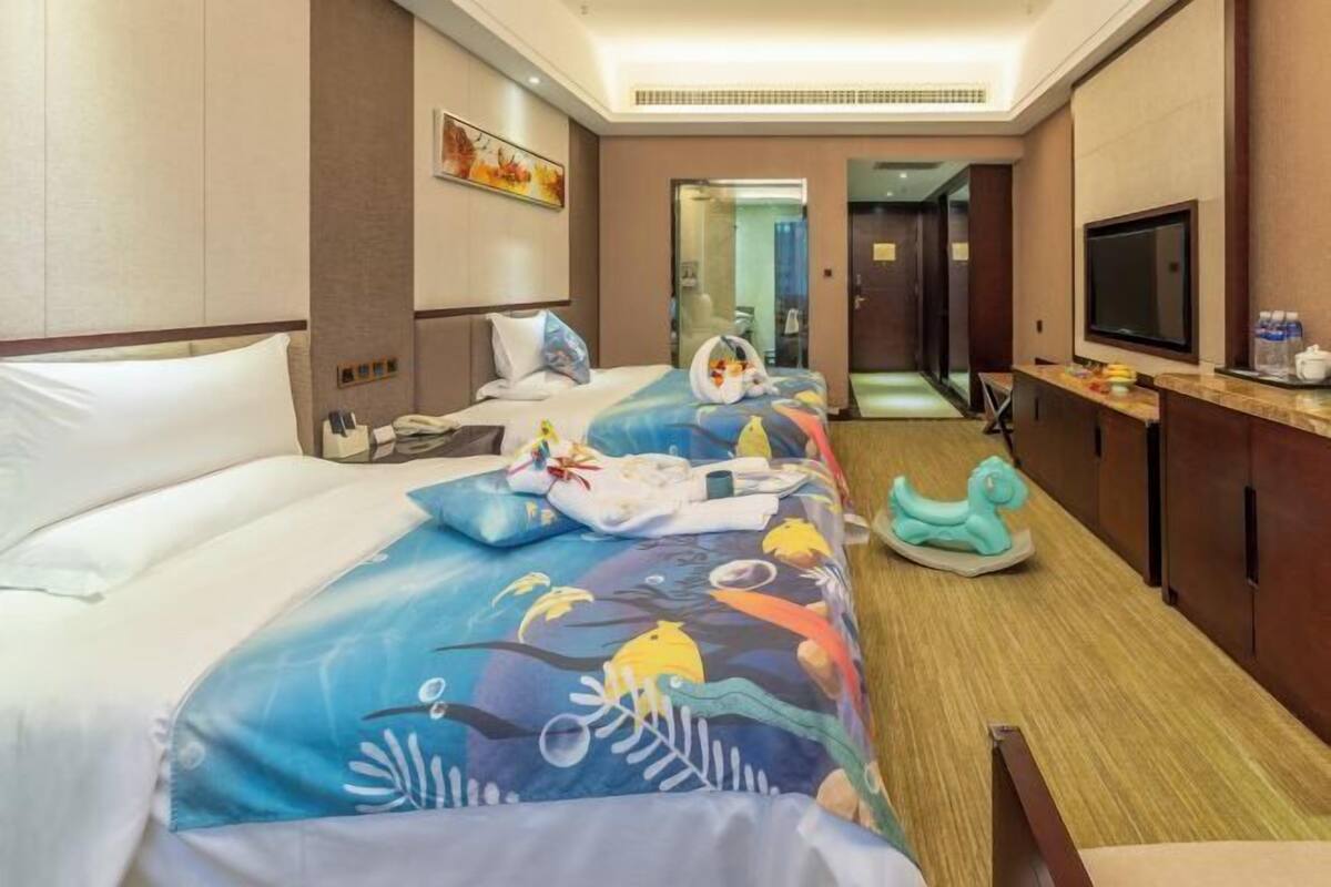 Quarto de hotel com uma cama, uma mesa de escritório, televisão e um banheiro visível ao fundo.