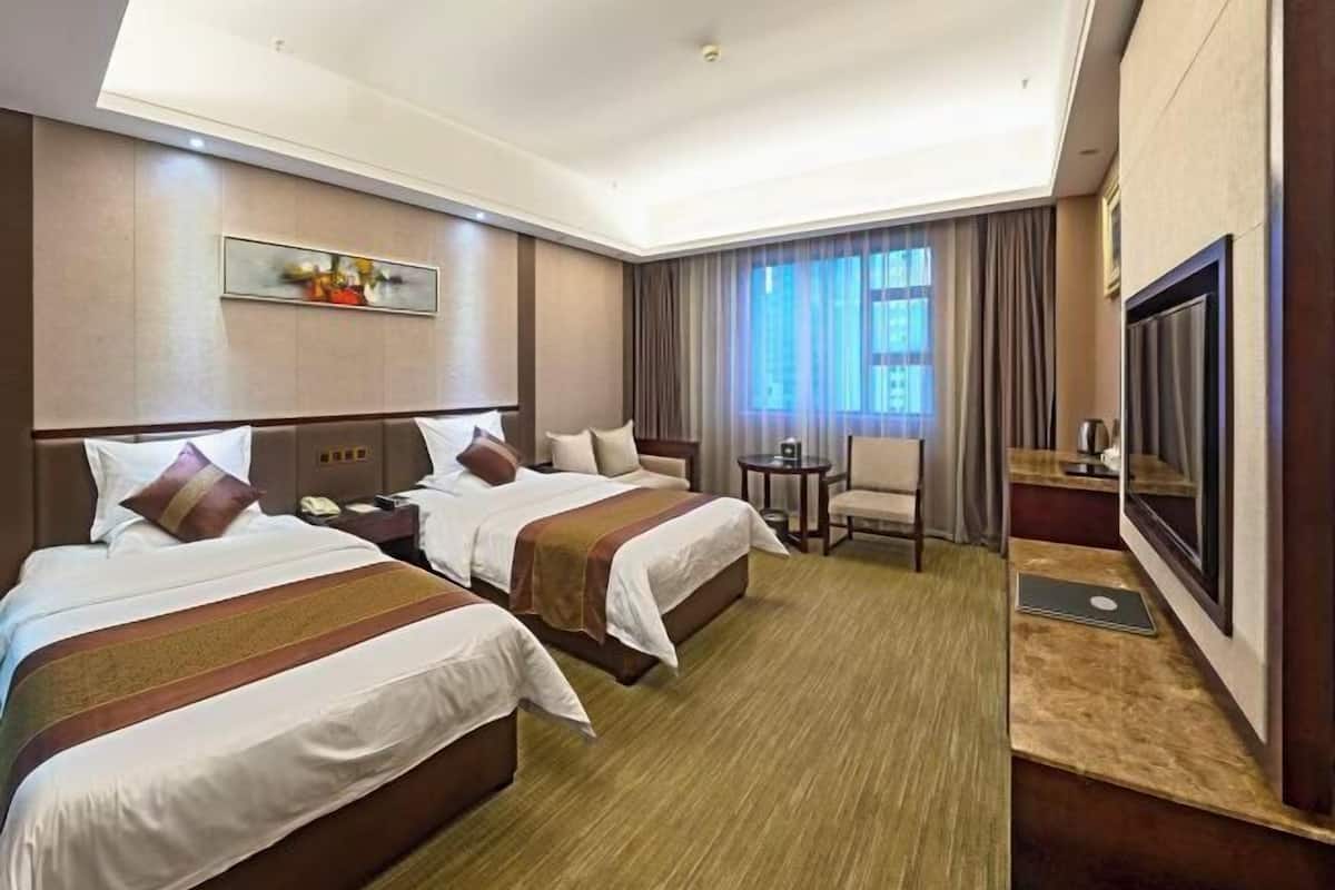Quarto de hotel com duas camas, uma escrivaninha, uma cadeira, televisão e uma janela grande com cortinas.