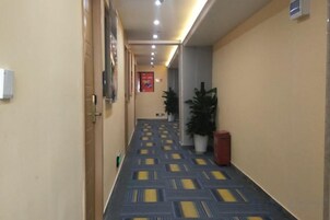 Corredor de hotel com carpete estampado, plantas em vasos e uma lixeira.