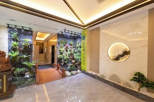 Um saguão de hotel com escadaria de madeira, balcão de recepção e parede com detalhe decorativo circular.