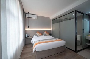 Quarto de hotel moderno com cama, mesa de cabeceira e closet envidraçado.