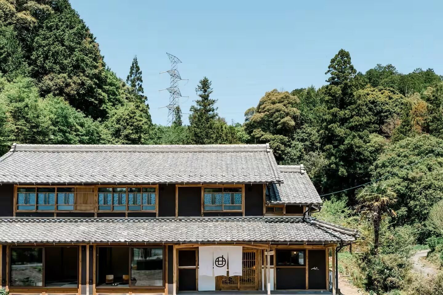 Um edifício tradicional japonês com telhado ladrilhado, janelas amplas e uma placa com caracteres japoneses.