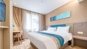 Quarto de hotel com cama, escrivaninha, cadeira e janela com cortinas.