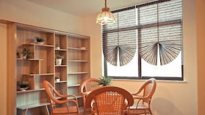 Quarto com estante de madeira, cadeiras de vime e uma grande janela com persianas.