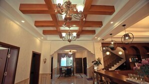 Um hall amplo com teto alto, vigas de madeira, um lustre e um bar com banquetas.