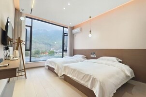 Quarto de hotel com duas camas, uma escrivaninha com cadeira, uma janela grande e vista para o exterior.