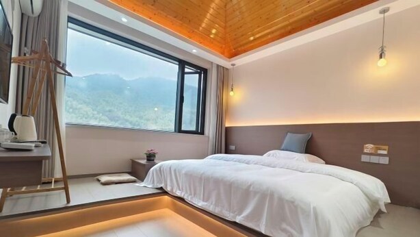 Quarto moderno com uma cama grande, teto de madeira, vista para montanhas e mesa de cabeceira com luminária.