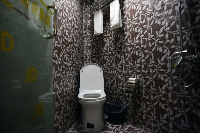 Casa de banho com sanita, chuveiro e parede estampada.