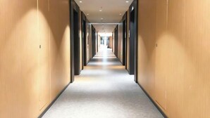 Um corredor comprido e estreito com paredes de madeira e piso coberto por carpete, que leva a um quarto claro no final.
