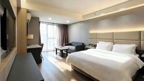 Quarto de hotel com cama, escrivaninha, cadeira, televisão e janela com cortinas.
