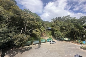 Estacionamento com um carro, cercado por árvores densas e um céu limpo.