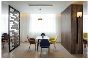 Uma área de refeições com mesa e cadeiras, uma divisória com padrão geométrico e uma luminária fixada na parede.