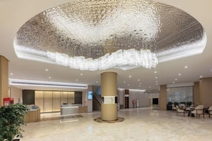 Um hall espaçoso com um detalhe circular grande no teto, balcão de recepção e área de estar.