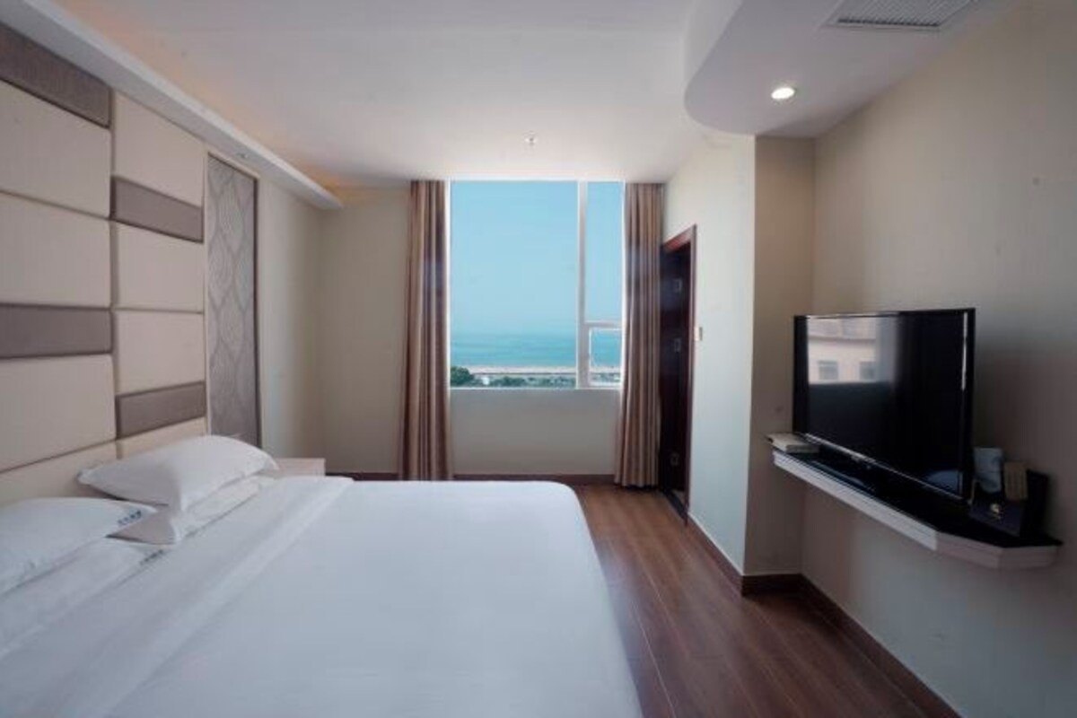 Quarto de hotel com uma cama, uma televisão, uma janela com vista e uma porta.