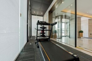 Espaço de ginástica com esteira, máquina de pesos e equipamentos de exercícios.