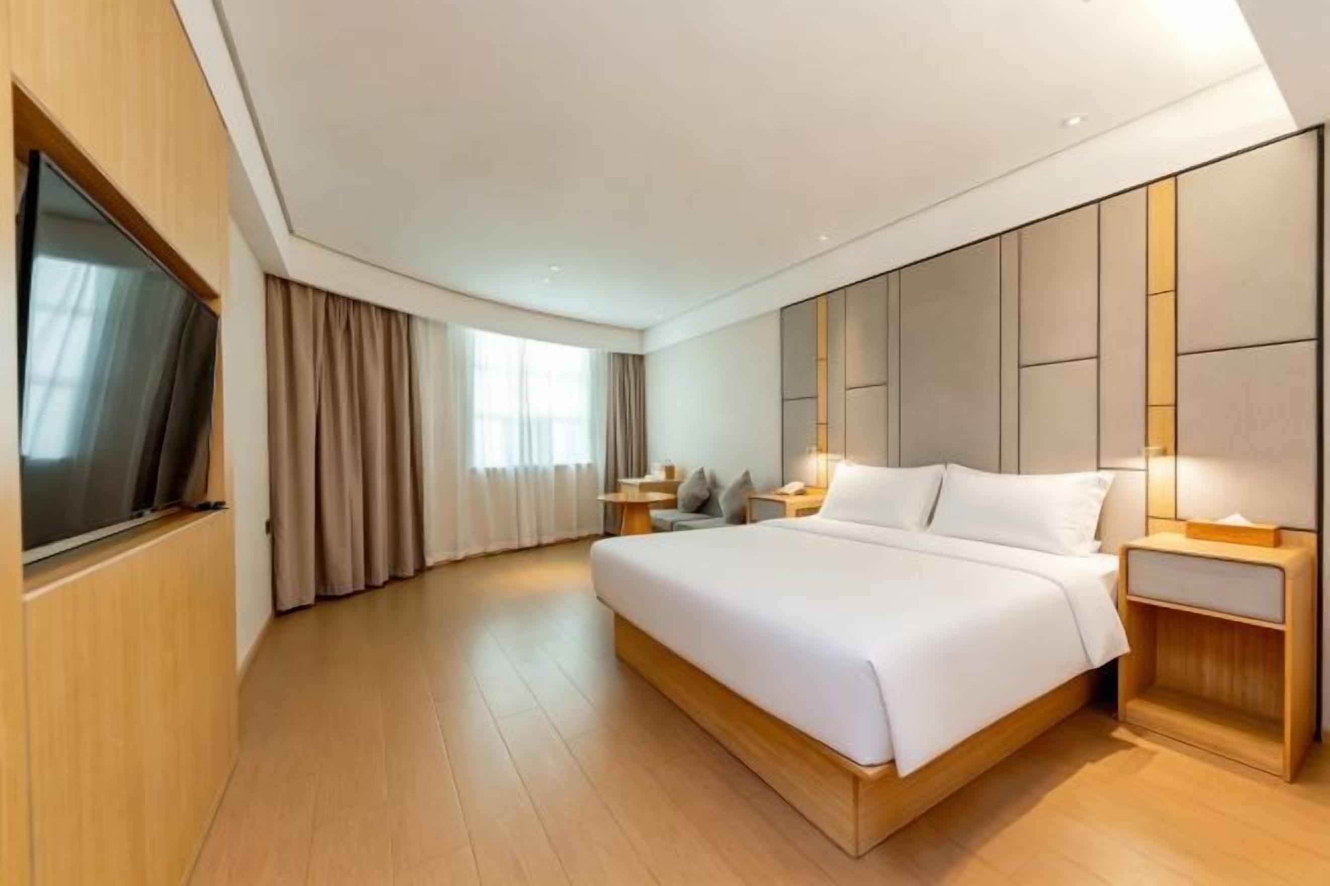 Quarto de hotel moderno com uma cama grande, mesas de cabeceira, uma TV e uma janela com cortinas.