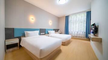 Quarto de hotel com duas camas, televisão, escrivaninha e janela com cortinas.