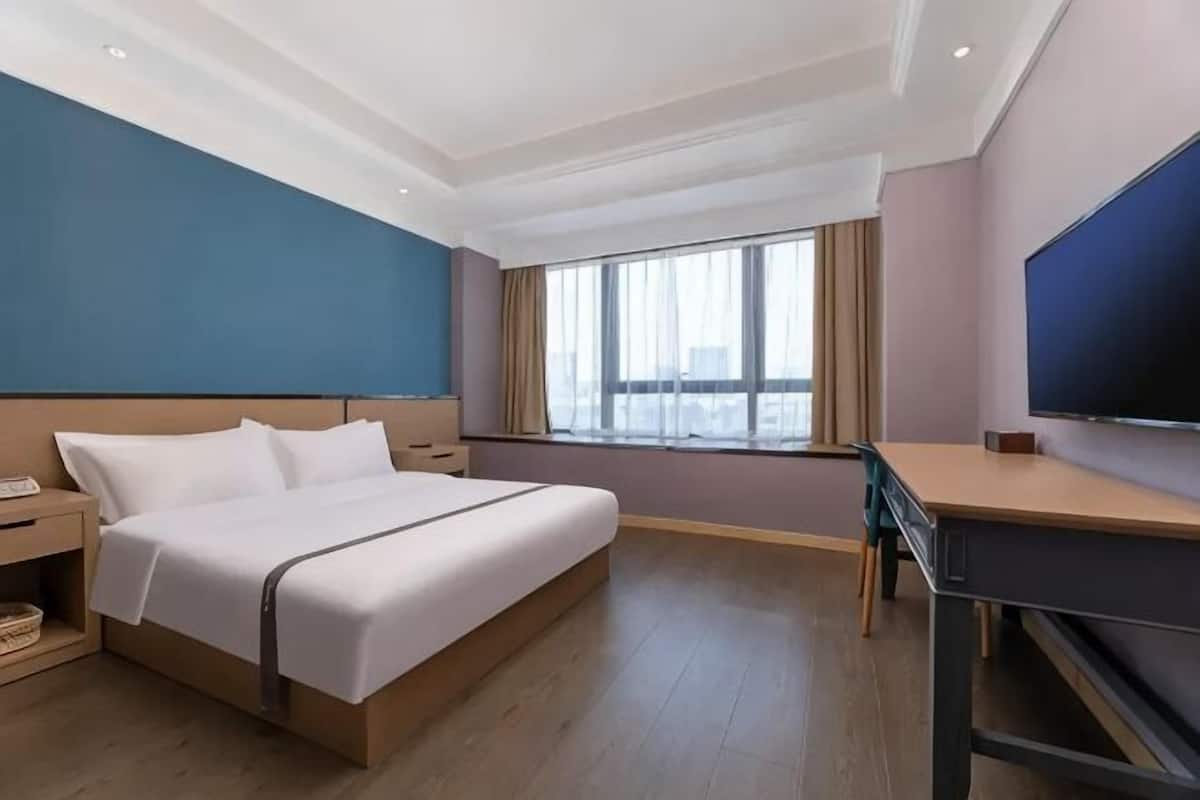 Quarto de hotel com cama, escrivaninha e janela grande.