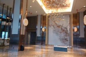 Um hall com parede de mármore, um lustre moderno e um balcão de recepção.