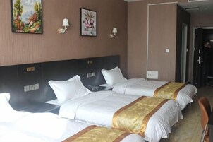 Quarto de hotel com duas camas, cabeceira, luminárias fixadas na parede e porta que dá para outro cômodo.