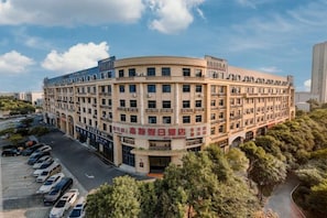 Um hotel de vários andares com fachada curva, estacionamento e área ajardinada com árvores.