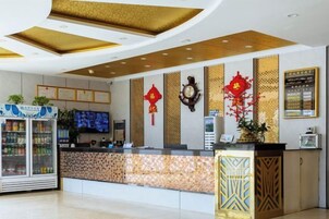 Área de recepção de hotel com balcão, televisão, frigorífico e elementos decorativos.