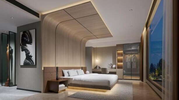 Quarto moderno com uma cama grande, mesas de cabeceira, luminária na parede e uma janela ampla com vista.