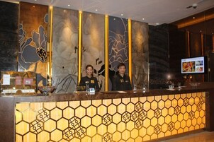 Uma mesa de recepção com padrão de colmeia, um grande mural com desenhos florais e uma tela de televisão.