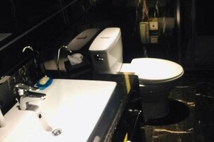 Casa de banho com lavatório branco, sanita e bancada de mármore preto.