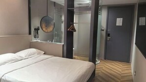 Quarto de hotel com uma cama, um espelho, uma porta e chão de madeira.