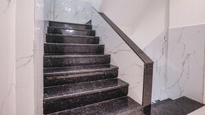 Uma escadaria com degraus de mármore preto e guarda-corpo de vidro, que leva a um andar superior.
