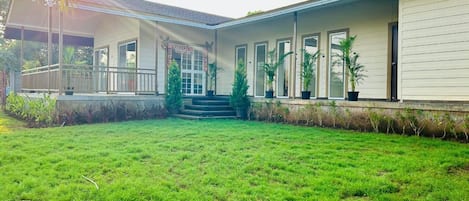 Uma casa de dois andares com varanda coberta, gramado e plantas em vasos.