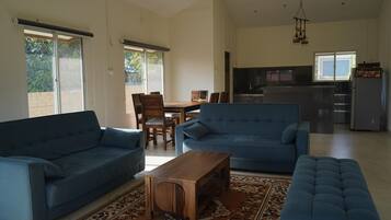 Uma sala de estar ampla com dois sofás azuis, uma mesa de centro de madeira e um tapete estampado.
