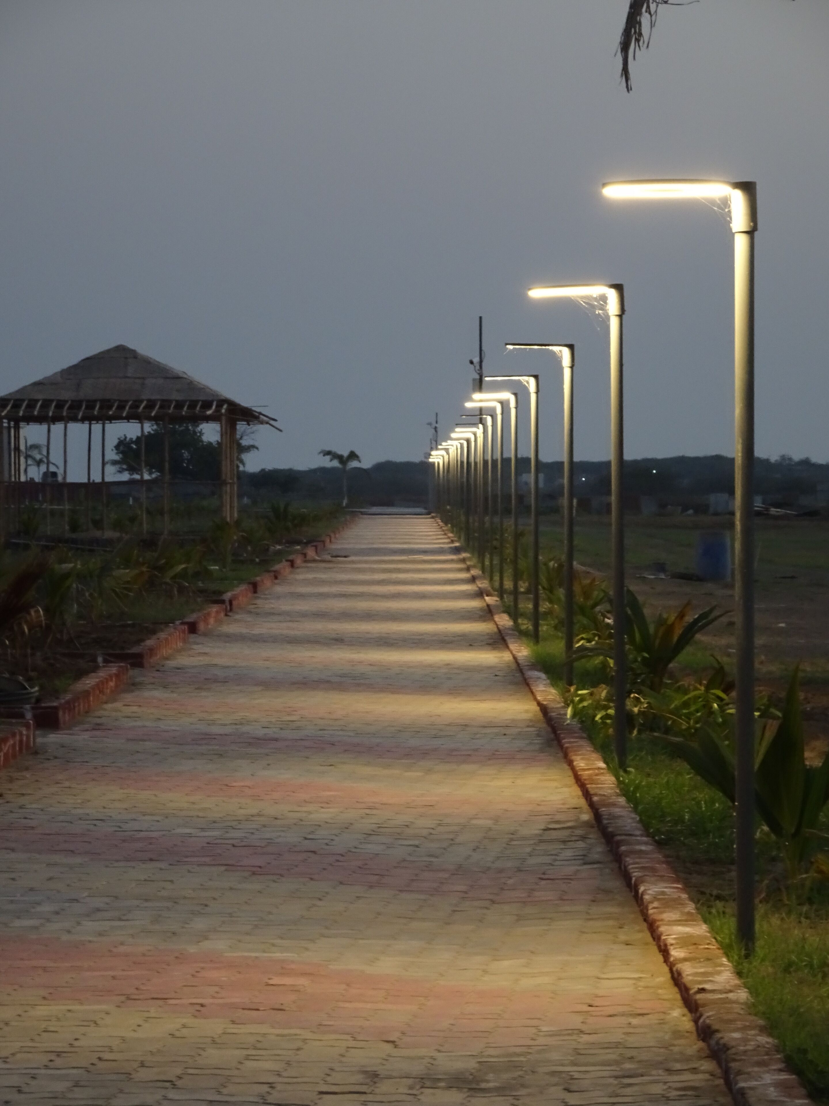 Um caminho pavimentado ladeado por postes de luz e um gazebo.