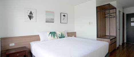 Quarto de hotel com uma cama grande, uma mesa de cabeceira de madeira, um guarda-roupa e duas obras de arte penduradas na parede.