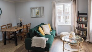 Uma sala de estar com um sofá verde, uma mesa de jantar de madeira e uma mesa de centro de vidro.