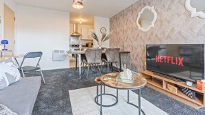 Uma sala de estar moderna com televisão de tela plana, área de jantar e cozinha ao fundo.