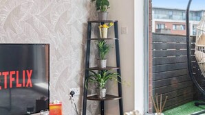 Sala de estar com televisão, prateleira de plantas e vista para um edifício.
