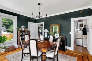 Uma sala de jantar com mesa e cadeiras de madeira, um lustre e vista para o exterior.