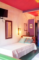 Quarto pequeno e acolhedor com uma cama de solteiro, um espelho, uma luminária na parede e uma porta que dá para outro cômodo.