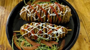 Uma frigideira preta com dois hambúrgueres grelhados, cobertos por um molho em formato de grade, e decorados com alface picada e rodelas de tomate.